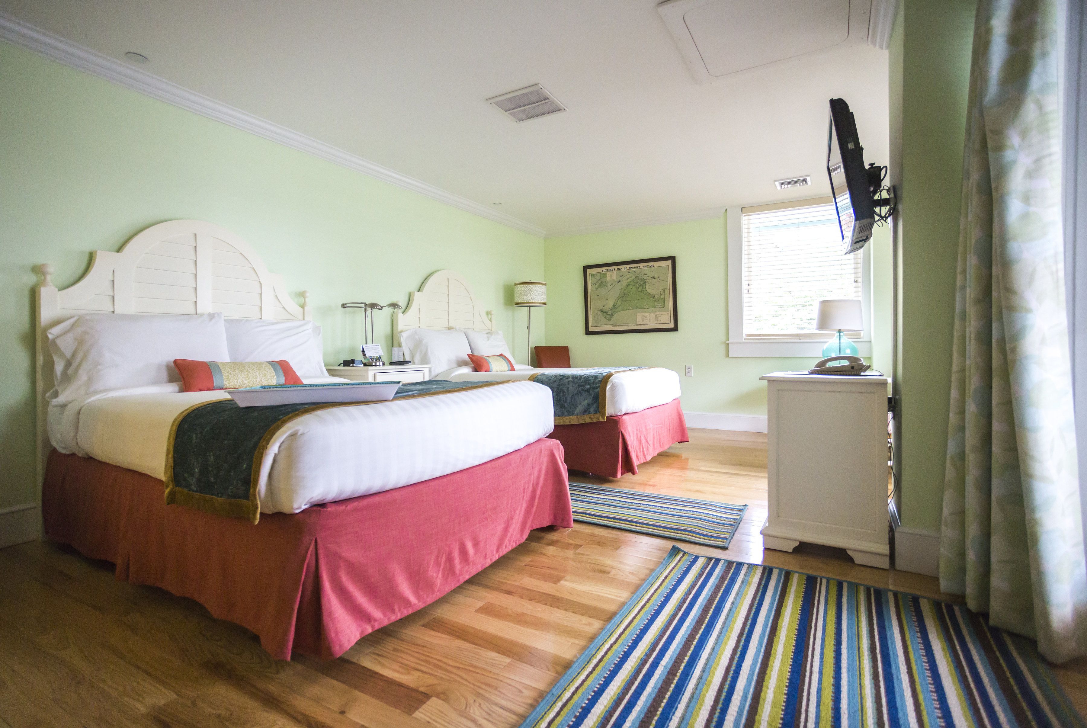Quarto de hotel com duas camas, uma escrivaninha, televisão de tela plana e janela com cortinas.