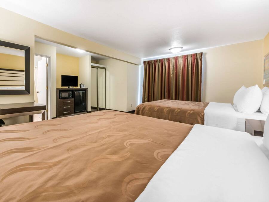 Quarto de hotel com duas camas, uma escrivaninha, televisão e porta de acesso a um banheiro.