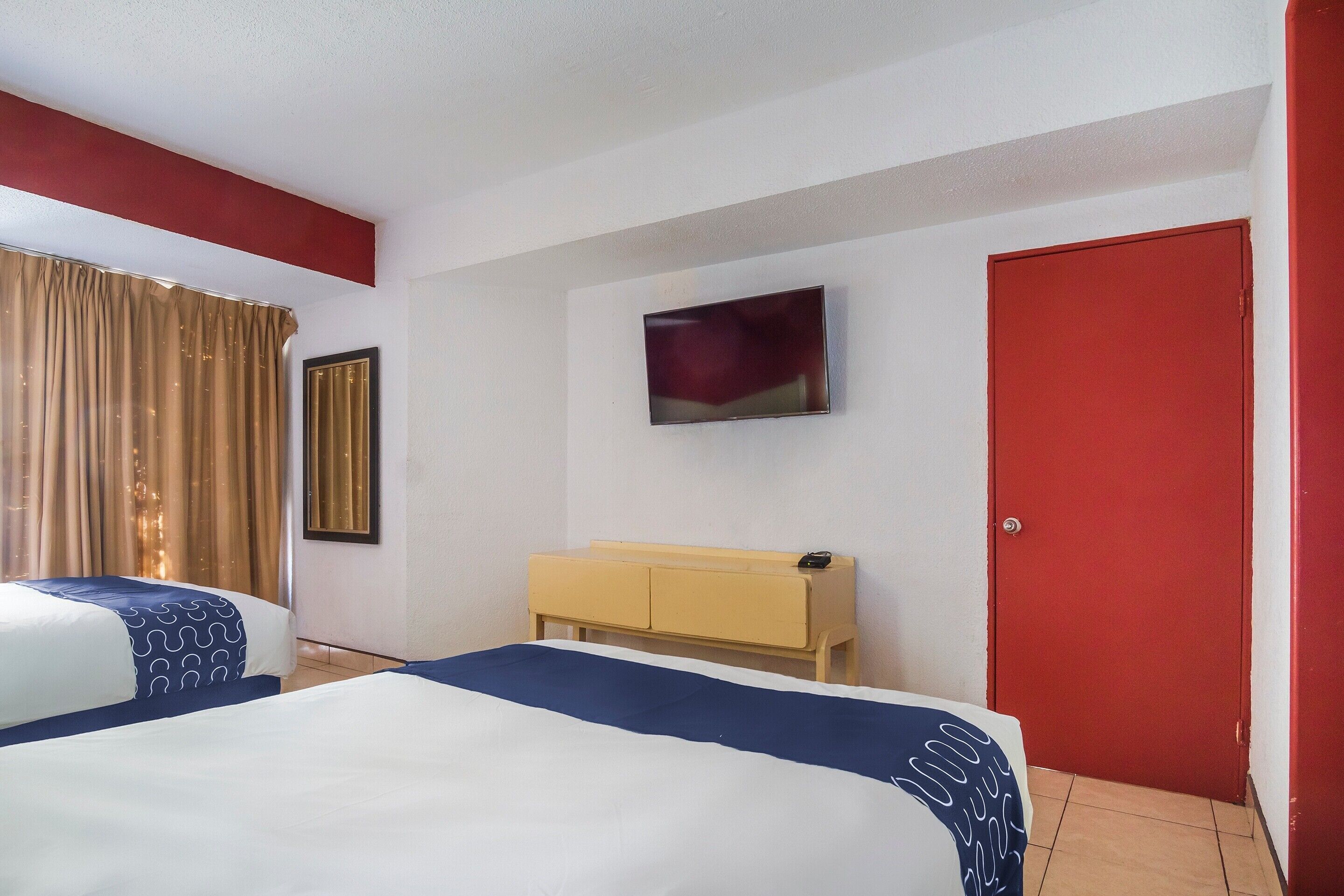 Quarto de hotel com duas camas, uma televisão, uma porta vermelha e um armário bege.