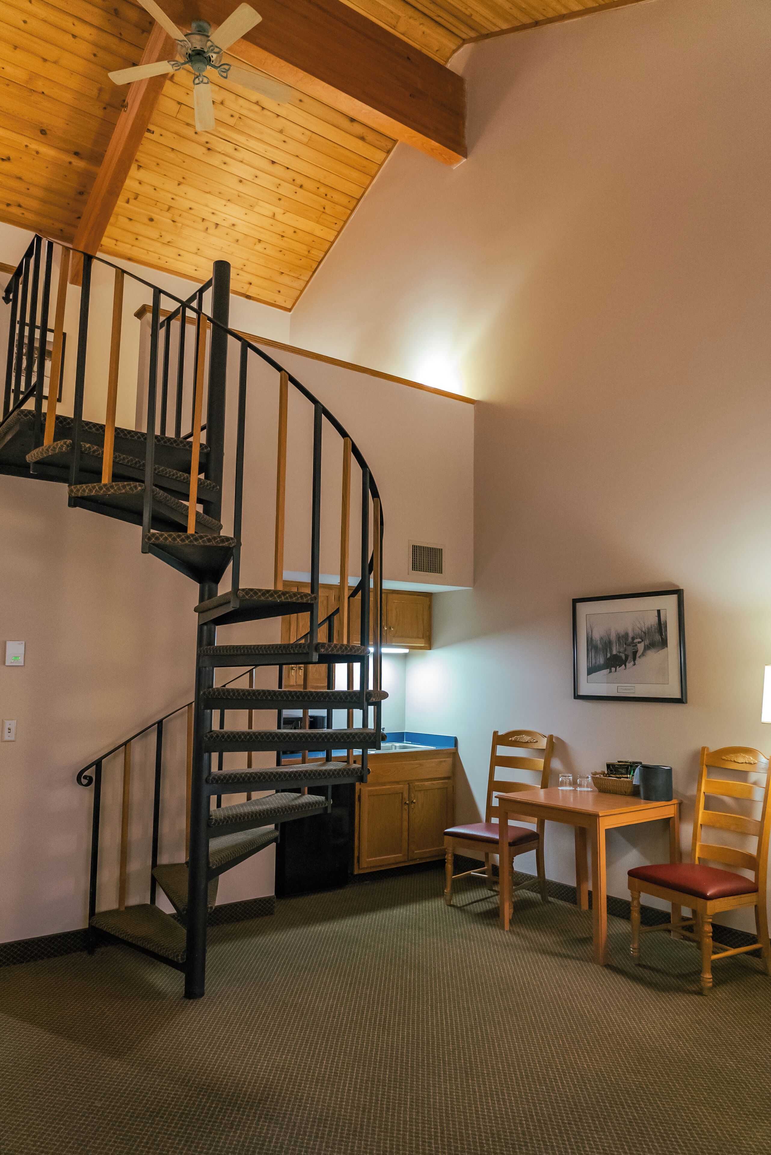 Uma escada em espiral com um ventilador de teto, uma sala de jantar com cadeiras e uma mesa, e um quadro na parede.