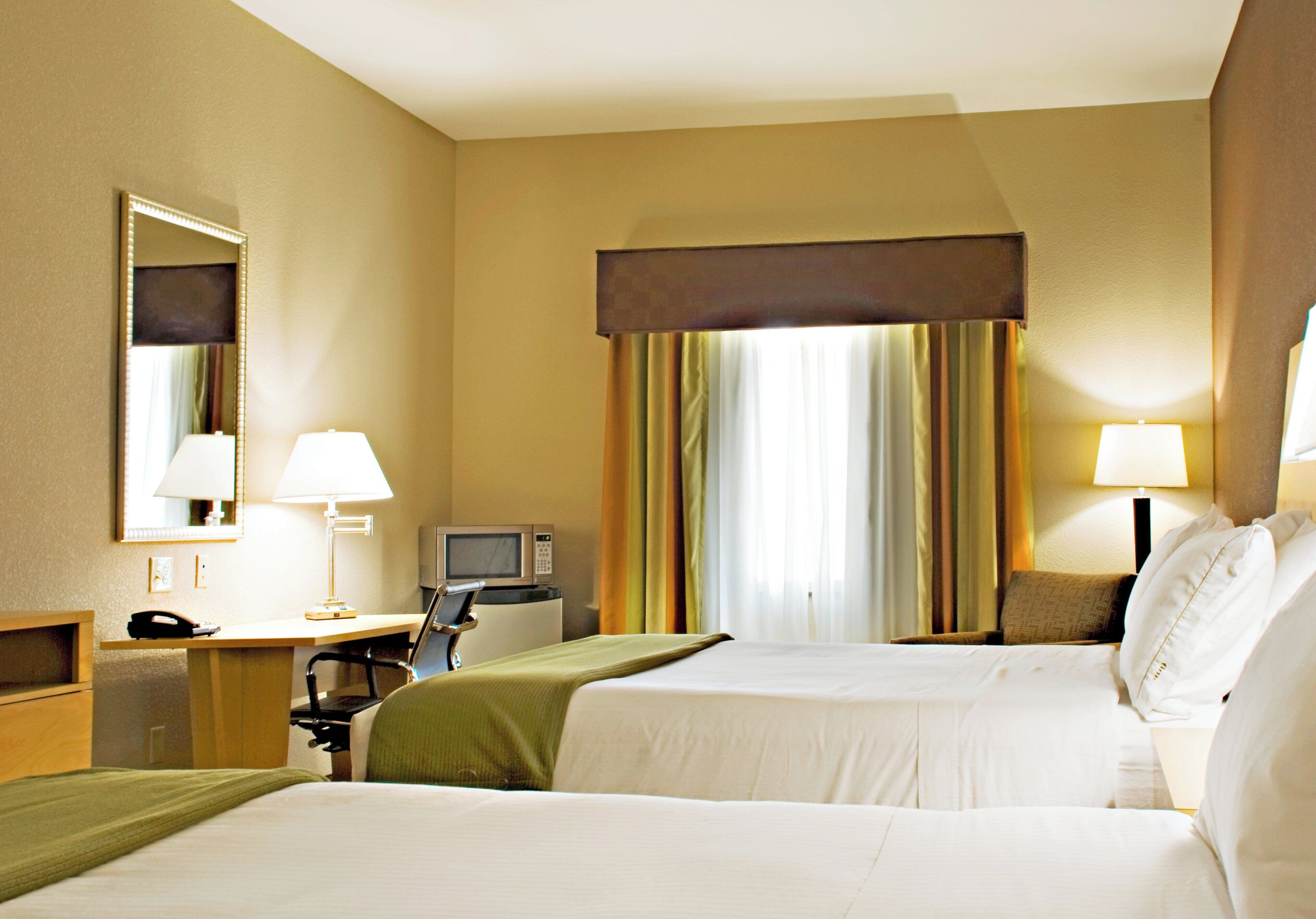 Quarto de hotel com duas camas, uma escrivaninha com telefone, televisão e janela com cortinas.