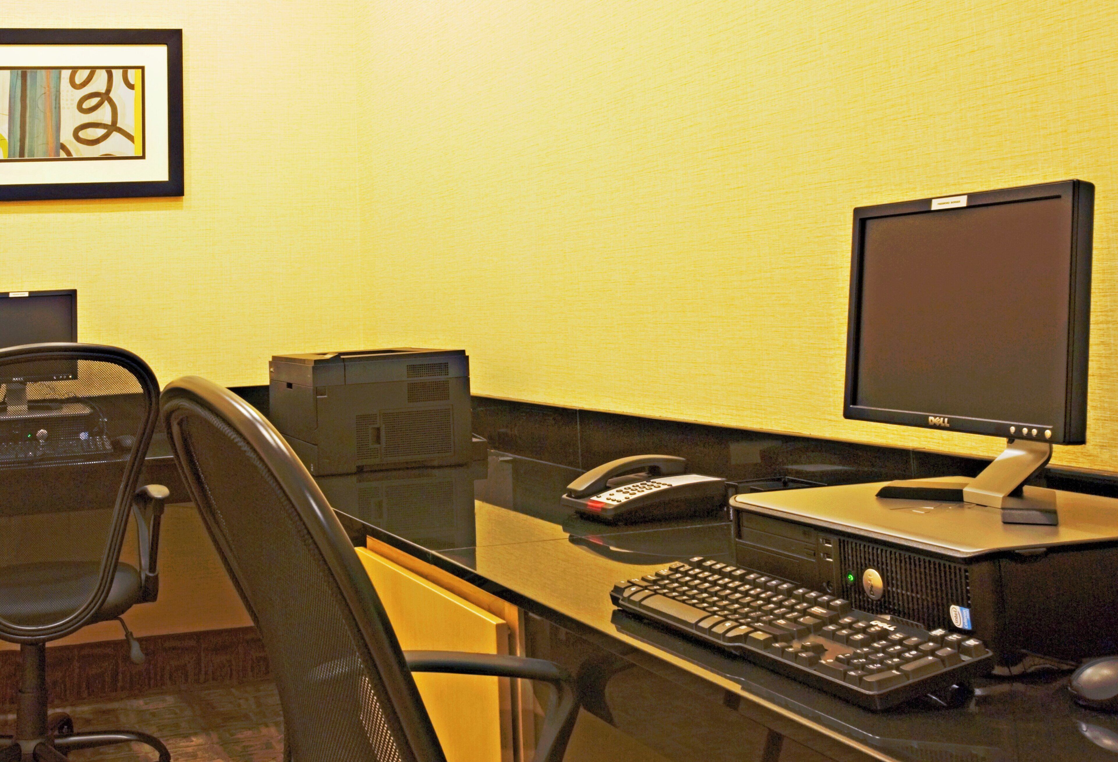 Quarto de hotel com escrivaninha, computador, telefone e cadeira.