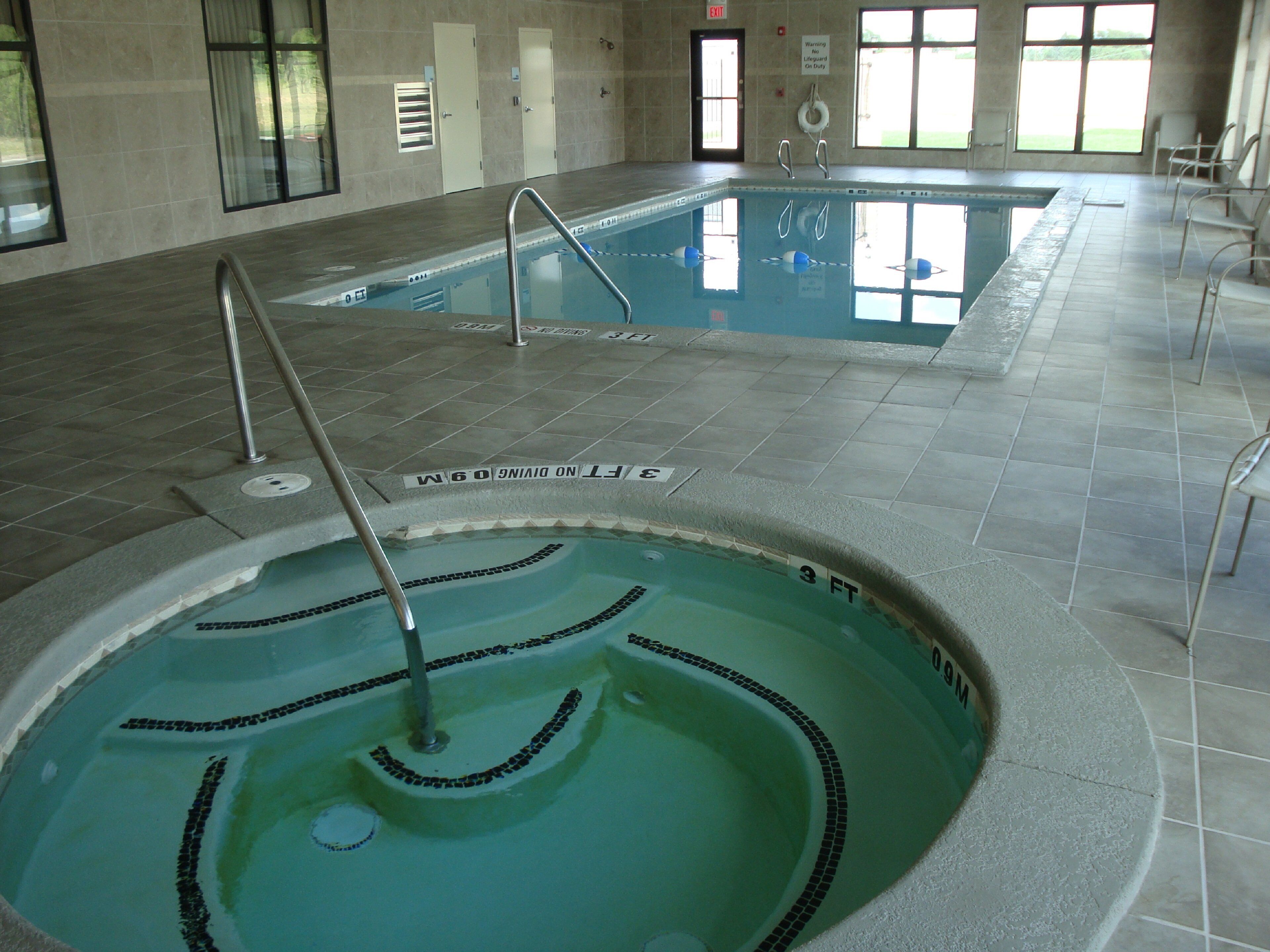Piscina interna com água cristalina, linhas de profundidade marcadas e posto de salva-vidas.
