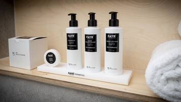 Uma prateleira com três frascos de condicionador, shampoo e loção corporal FAYR by WestCord, um sabonete em barra e uma caixa branca.