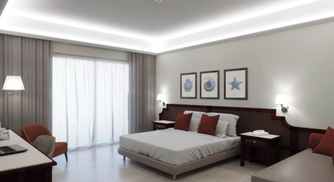 Quarto de hotel com uma cama grande, escrivaninha, cadeira, mesa de cabeceira e janela com cortinas.