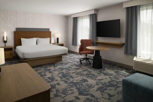 Quarto de hotel com cama, escrivaninha, cadeira, televisão e janela com cortinas.