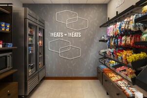 Interior de um supermercado com seções refrigeradas, corredores de lanches e uma parede com padrões hexagonais.