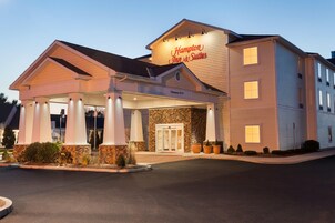 Um Hampton Inn & Suites com entrada coberta, detalhes em pedra e céu claro.