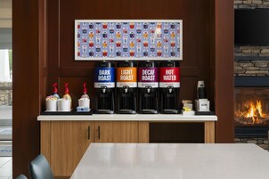 Estação de café com quatro dispensadores identificados como TORRA ESCURA, TORRA CLARA, DESCAFEINADO e ÁGUA QUENTE, e um expositor de xícaras de café na parede acima.