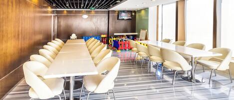 Uma sala de conferências com uma mesa comprida e cadeiras, uma televisão e uma área de recreação infantil com brinquedos e um escorregador.