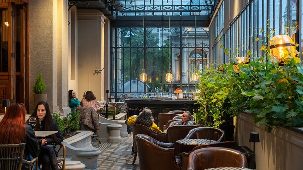 Um café com mesas ao ar livre, piso de azulejos e vista para a rua através de grandes janelas.