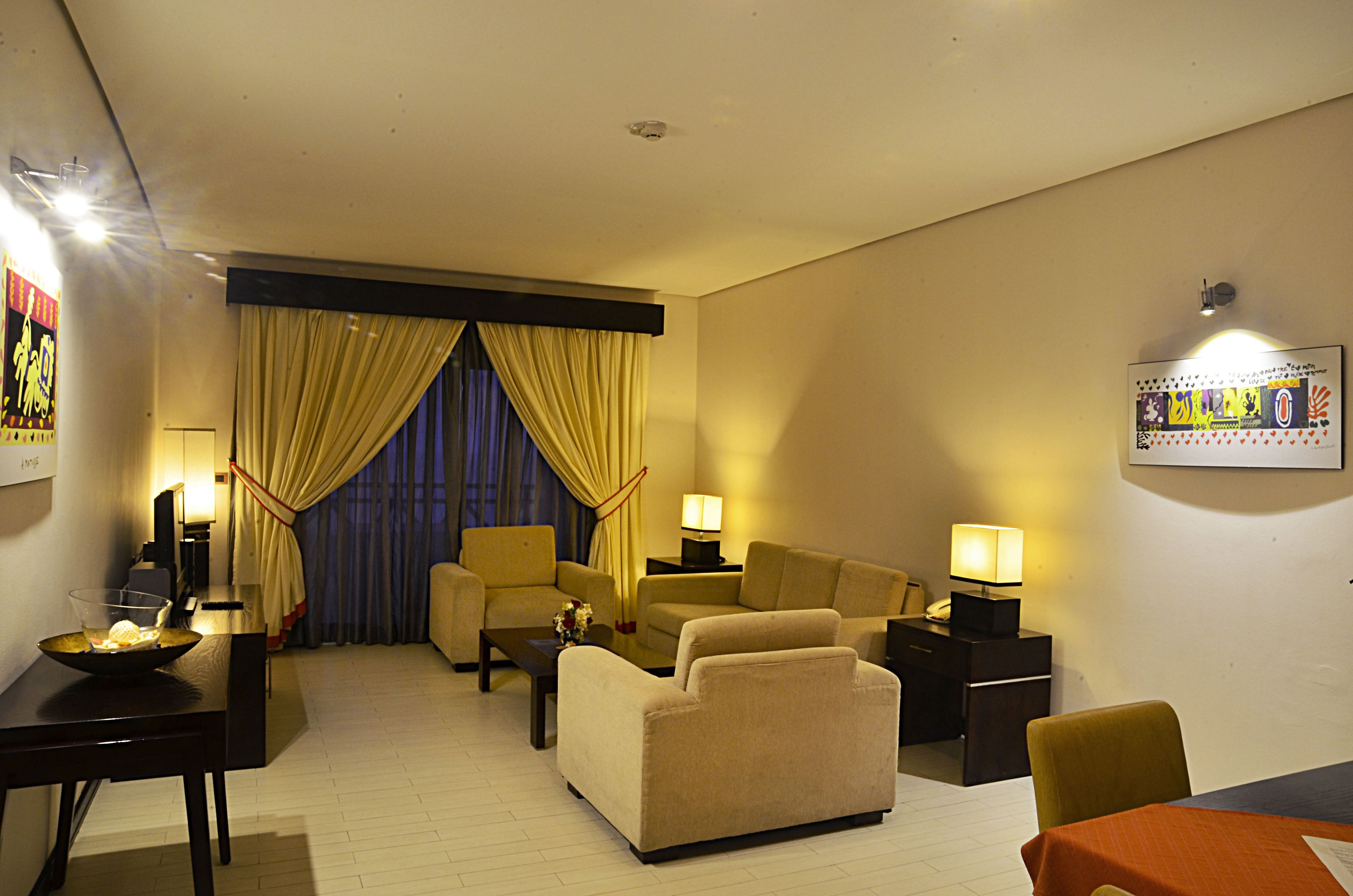 Quarto de hotel com sofás, uma mesa de jantar, uma mesa de centro e duas luminárias.