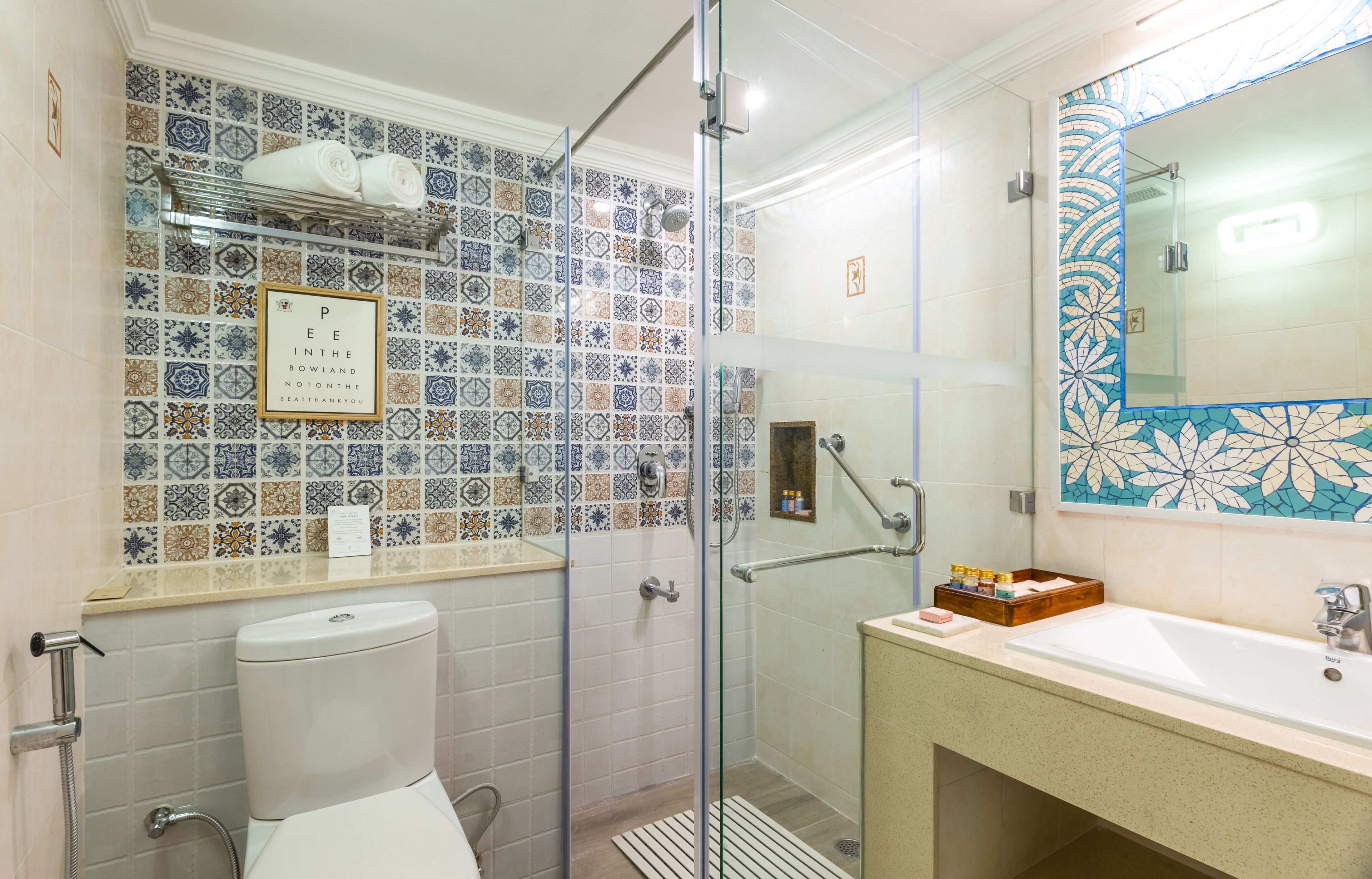 Casa de banho com chuveiro, sanita, lavatório e painel de azulejos decorativos.