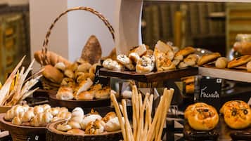 Diversos pães e doces dispostos em tábuas de madeira e uma grade de metal.