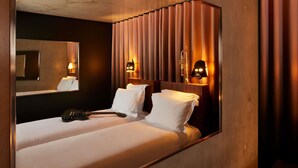 Quarto de hotel com uma cama grande, um espelho, duas luminárias de cabeceira e um violão sobre a cama.