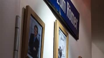 Paredes com uma placa indicando "Hotel Zum Romer" e diversas fotografias emolduradas.