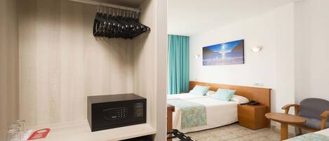 Quarto de hotel com cama, escrivaninha com micro-ondas, cadeira e mesa pequena.