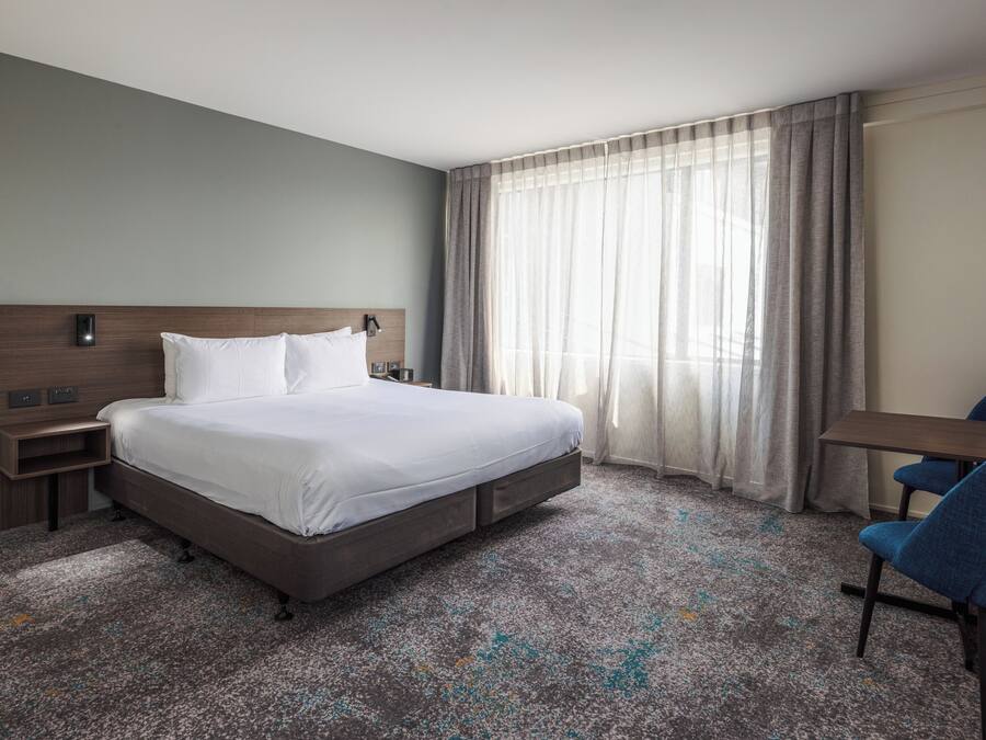 Quarto de hotel com uma cama grande, uma escrivaninha e uma cadeira.