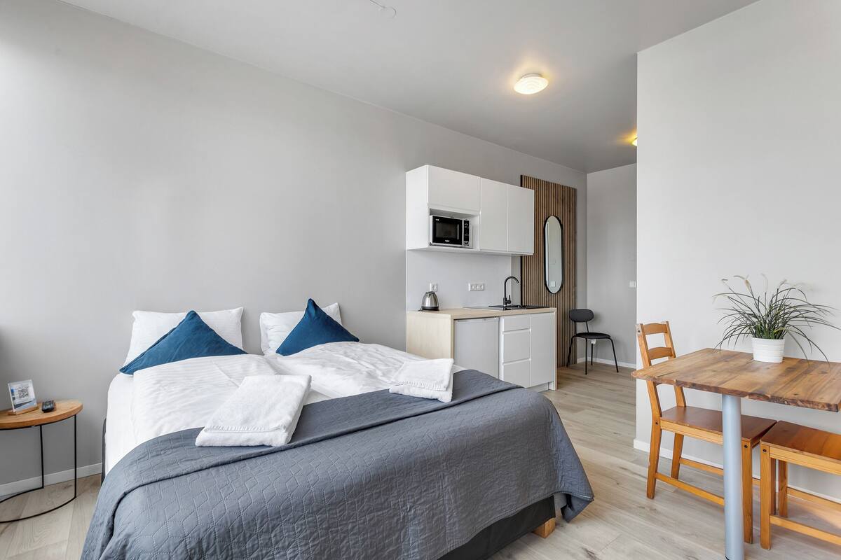 Quarto moderno com cama, mesa de cabeceira e um pequeno espaço de trabalho com cadeira.