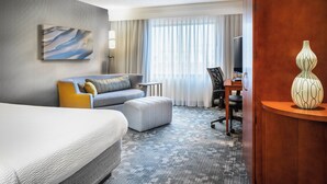 Quarto de hotel com uma cama grande, um sofá, um banquinho, uma escrivaninha e um abajur.