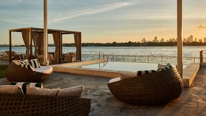Um lounge no terraço com móveis de vime, piscina e vista para o horizonte da cidade.
