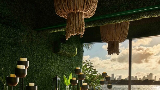 Uma longa mesa de jantar posta com cadeiras, uma parede verde e vista para o horizonte urbano.