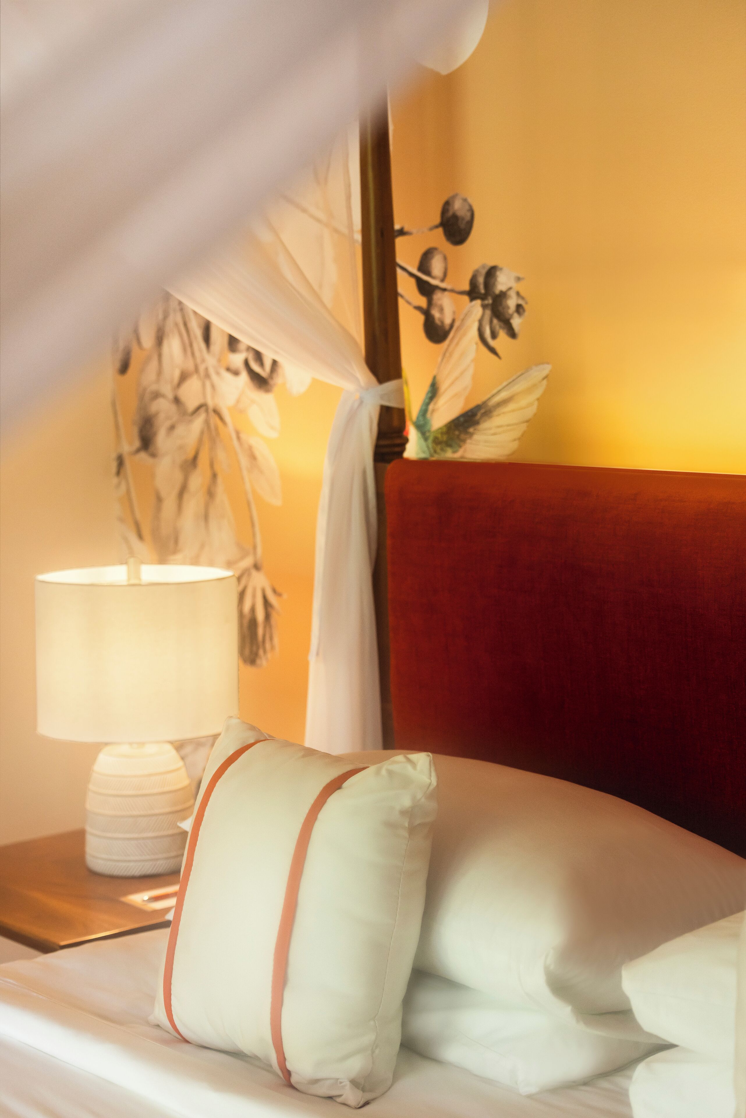 Quarto de hotel com uma cama, uma mesa de cabeceira com abajur e uma parede com um mural floral.