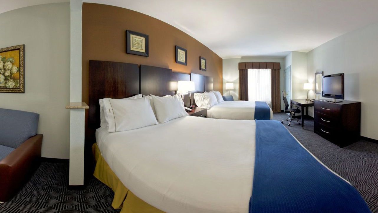 Quarto de hotel com duas camas, uma mesa, televisão e uma cadeira.