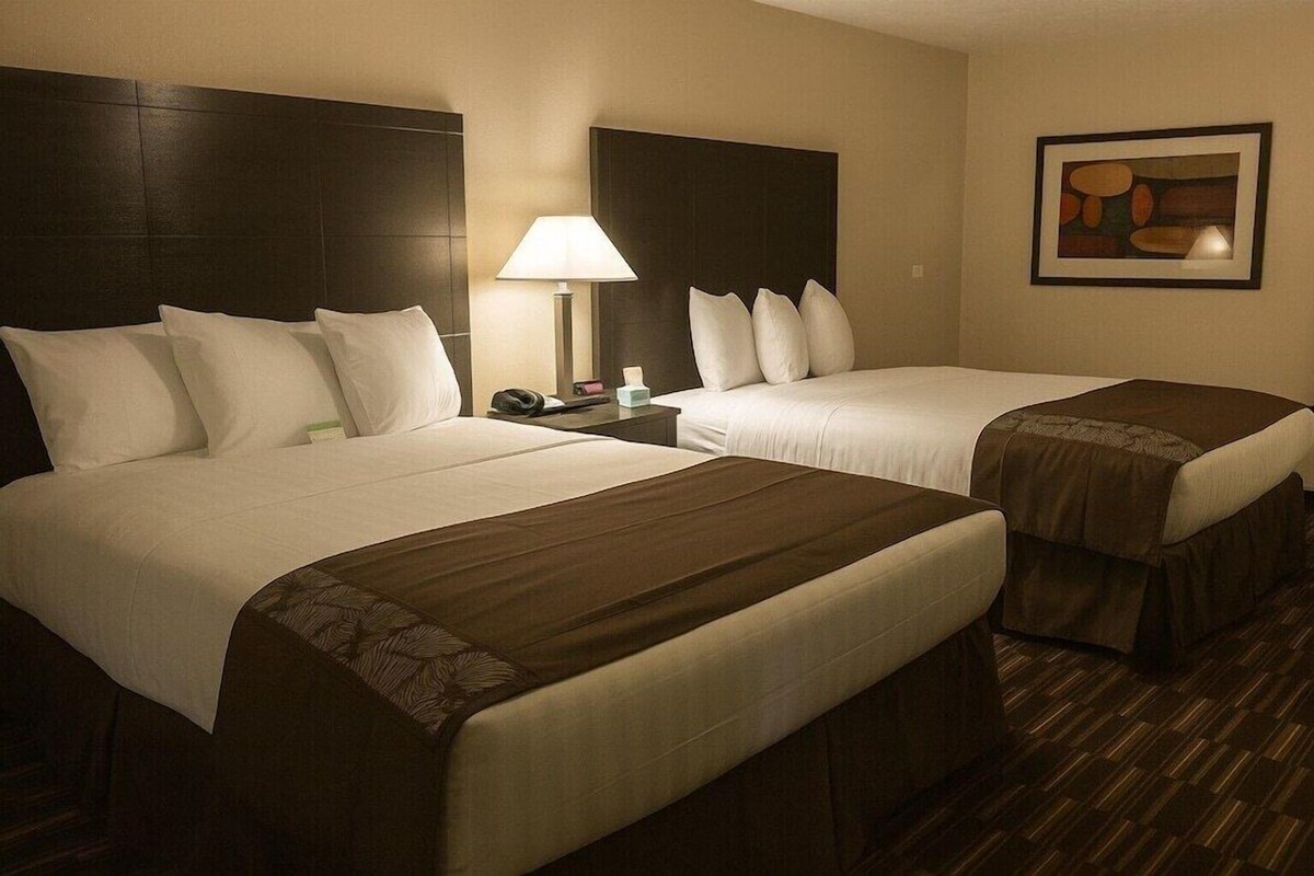 Quarto de hotel com duas camas, uma mesa de cabeceira, uma luminária e um quadro na parede.