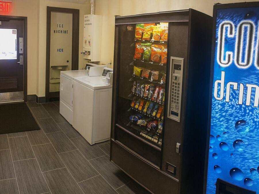Máquina de vendas com placa 'Cold Drink', máquina de lavar e placa de saída em um corredor.
