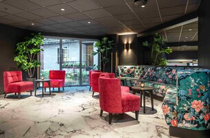 Um espaço interno moderno com cadeiras vermelhas, um sofá floral e piso de mármore.