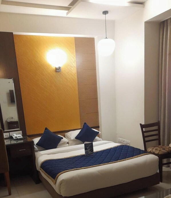 Quarto de hotel com cama, escrivaninha, cadeira e mesa de cabeceira.