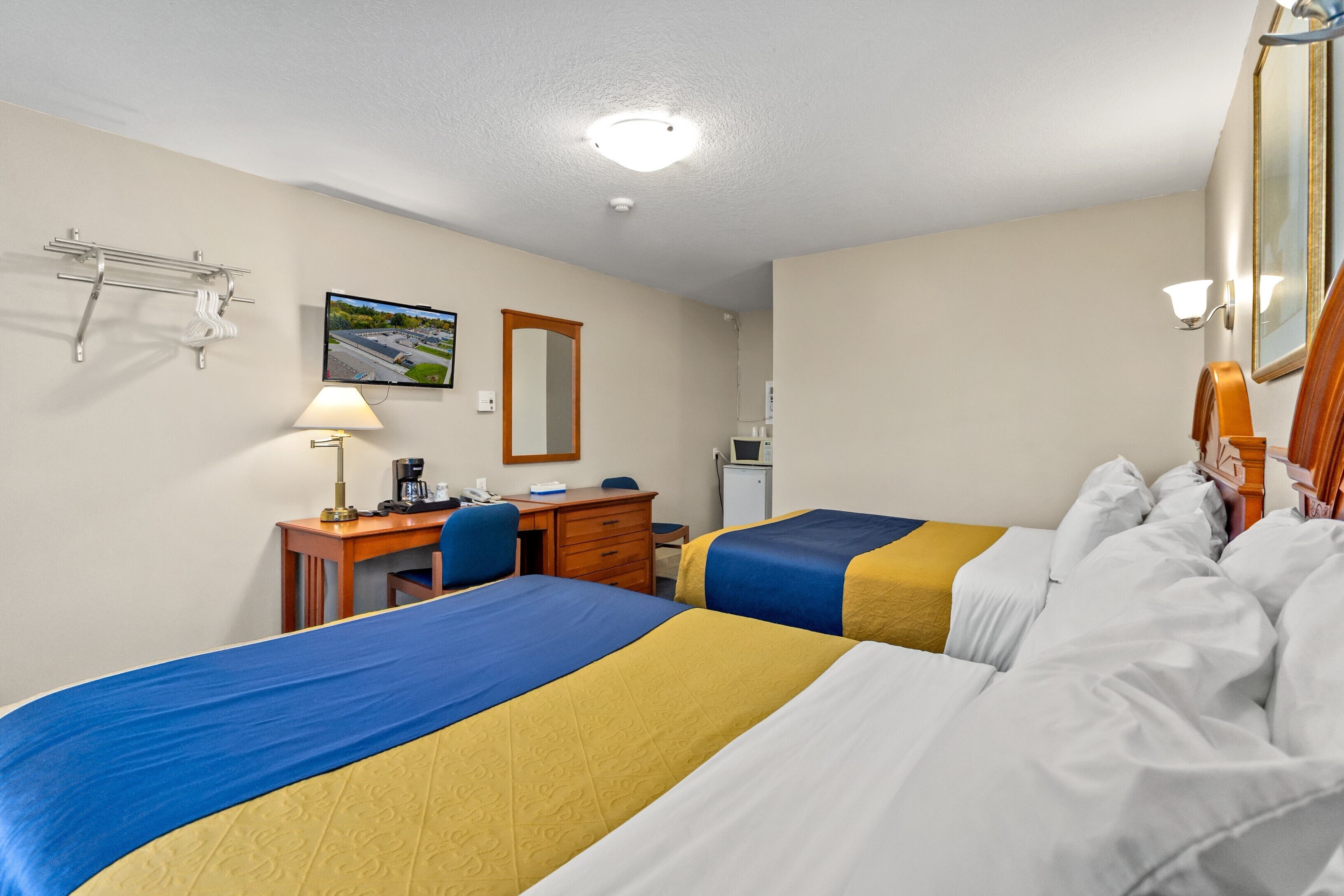 Quarto de hotel com duas camas, uma escrivaninha, uma cadeira, uma televisão e um espelho.