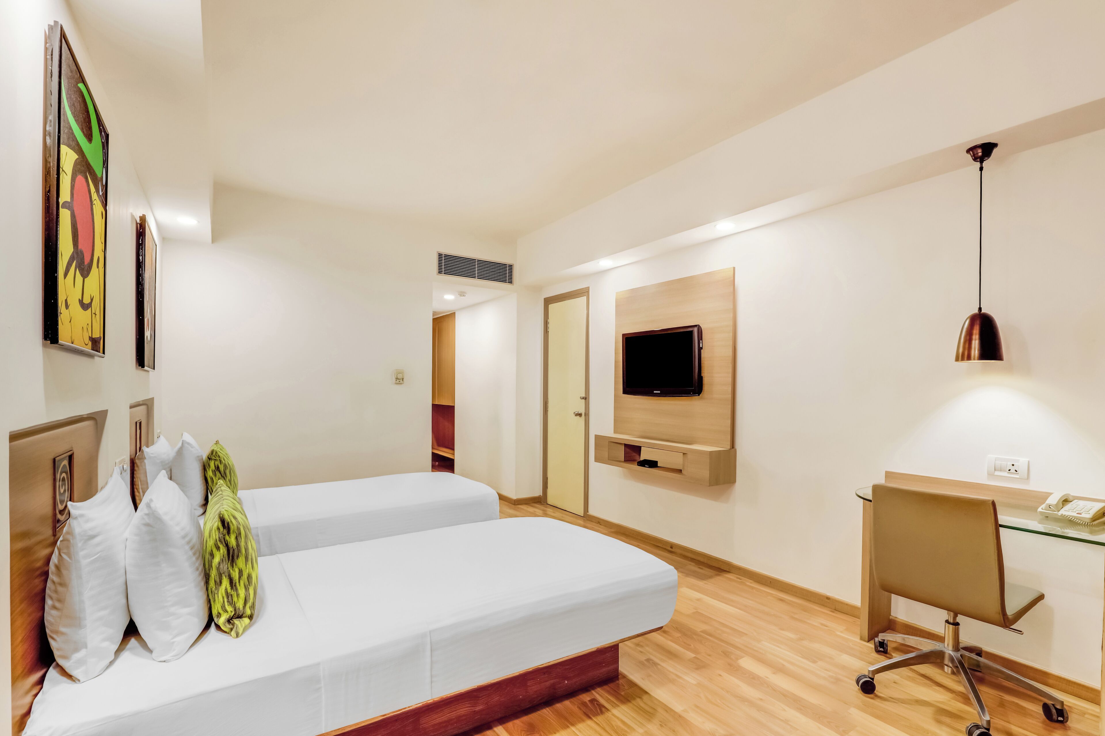 Quarto de hotel com duas camas, uma escrivaninha, televisão e uma cadeira.
