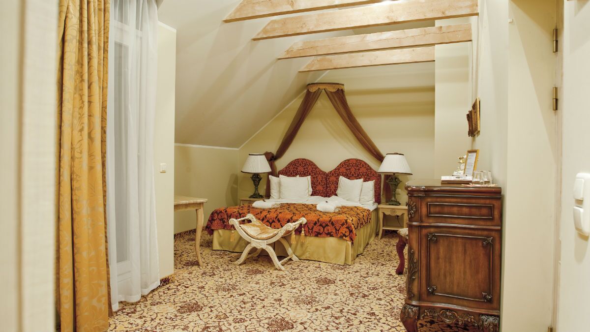 Quarto com cama, duas mesas de cabeceira, um criado-mudo, um armário de madeira e uma cadeira decorativa.