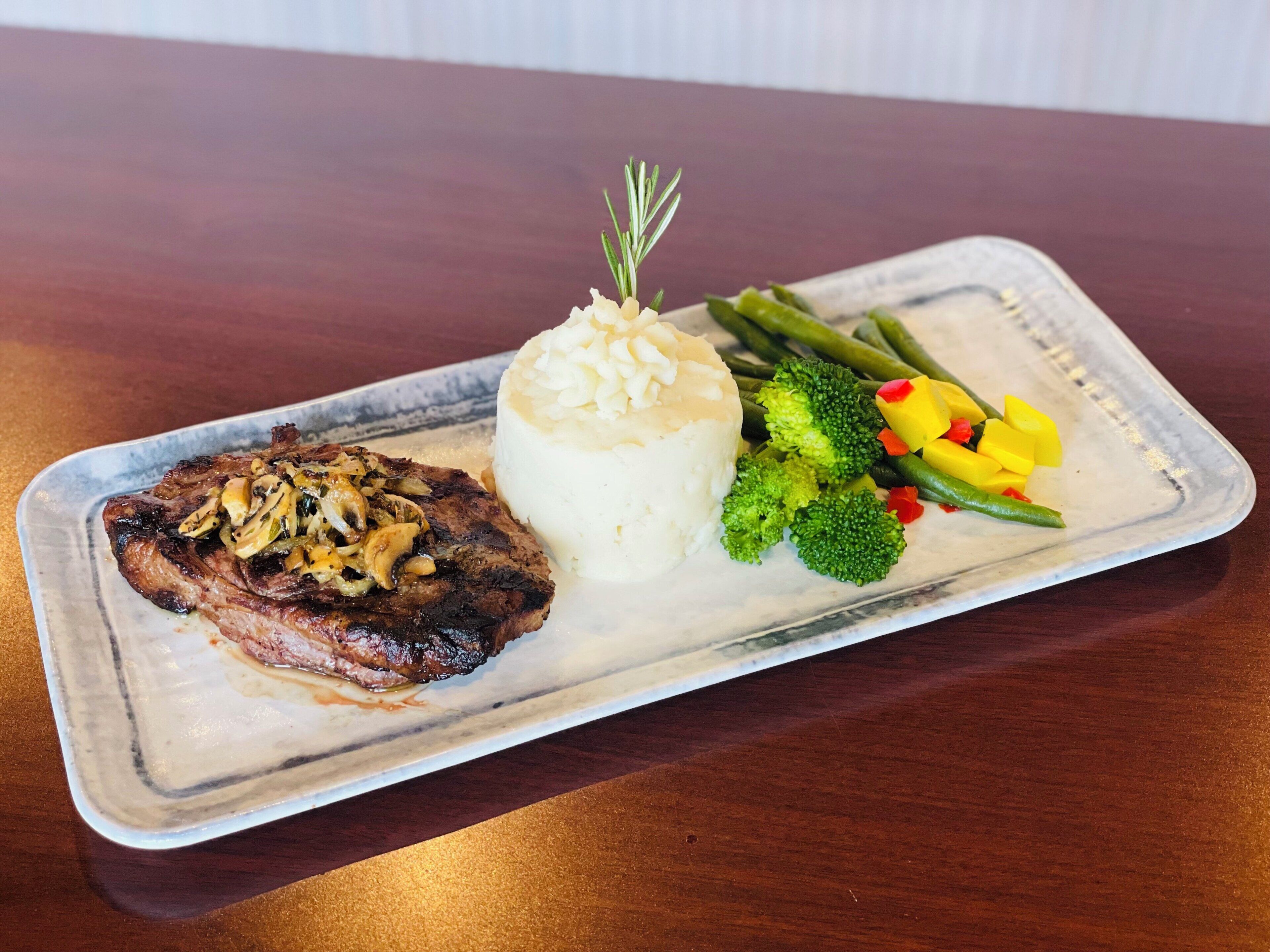 Um prato com bife, purê de batata, brócolis e vagem.