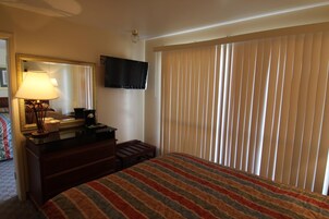 Quarto de hotel com cama, penteadeira, espelho, televisão e janela com persianas.