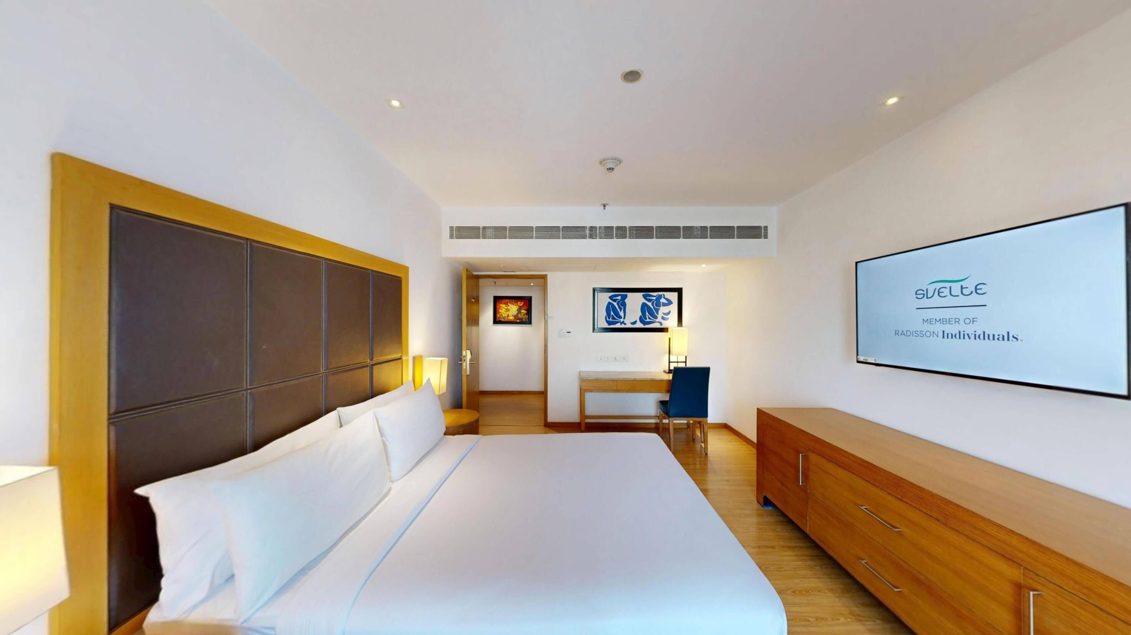 Quarto de hotel moderno com uma cama grande, uma mesa e uma televisão.
