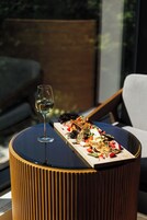 Uma mesa com uma taça de vinho branco e uma tábua de petiscos variados.