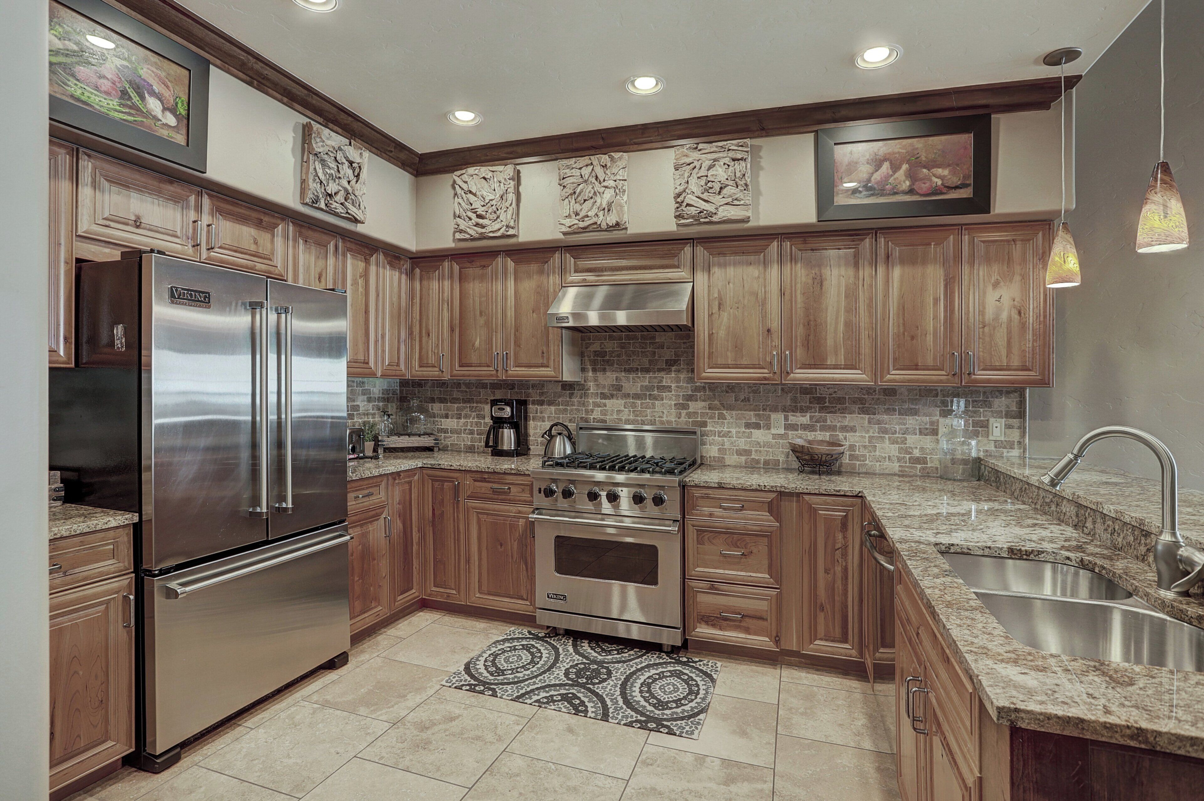 Uma cozinha com armários de madeira, eletrodomésticos de aço inoxidável, backsplash de tijolos e bancada de granito.