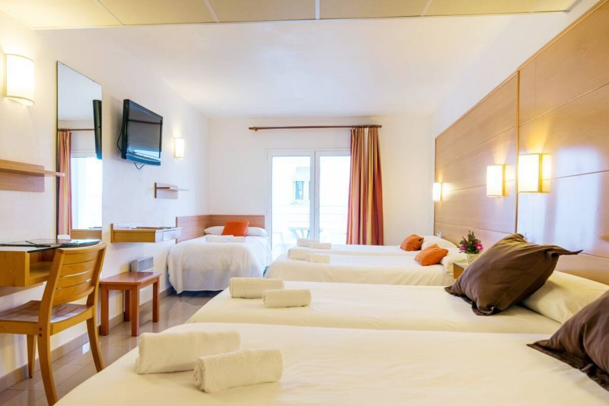 Quarto de hotel com duas camas, uma escrivaninha, uma cadeira, uma televisão e uma janela com cortinas.