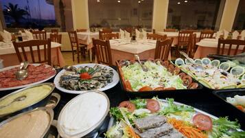 Buffet com diversos pratos, incluindo carnes, frutos do mar, saladas e patês.