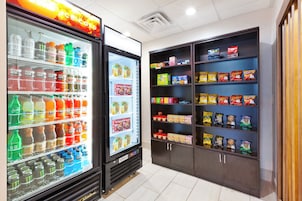 Máquina automática com diversas bebidas e lanches, e uma prateleira repleta de produtos embalados.