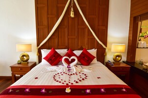 Quarto de hotel com cama, duas mesas de cabeceira, um criado-mudo, espelho e cabeceira de madeira.