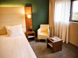 Quarto de hotel com cama, poltrona, mesa pequena, mesa de cabeceira e abajur.