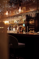 Uma área de bar com vários copos de vinho pendurados, um monitor de computador e diversas garrafas.