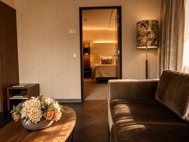 Quarto de hotel com sofá, uma pequena mesa com um arranjo floral, cama com cabeceira e abajur com design floral.