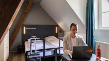 Quarto de hotel moderno com cama beliche, escrivaninha com um laptop e uma mala.