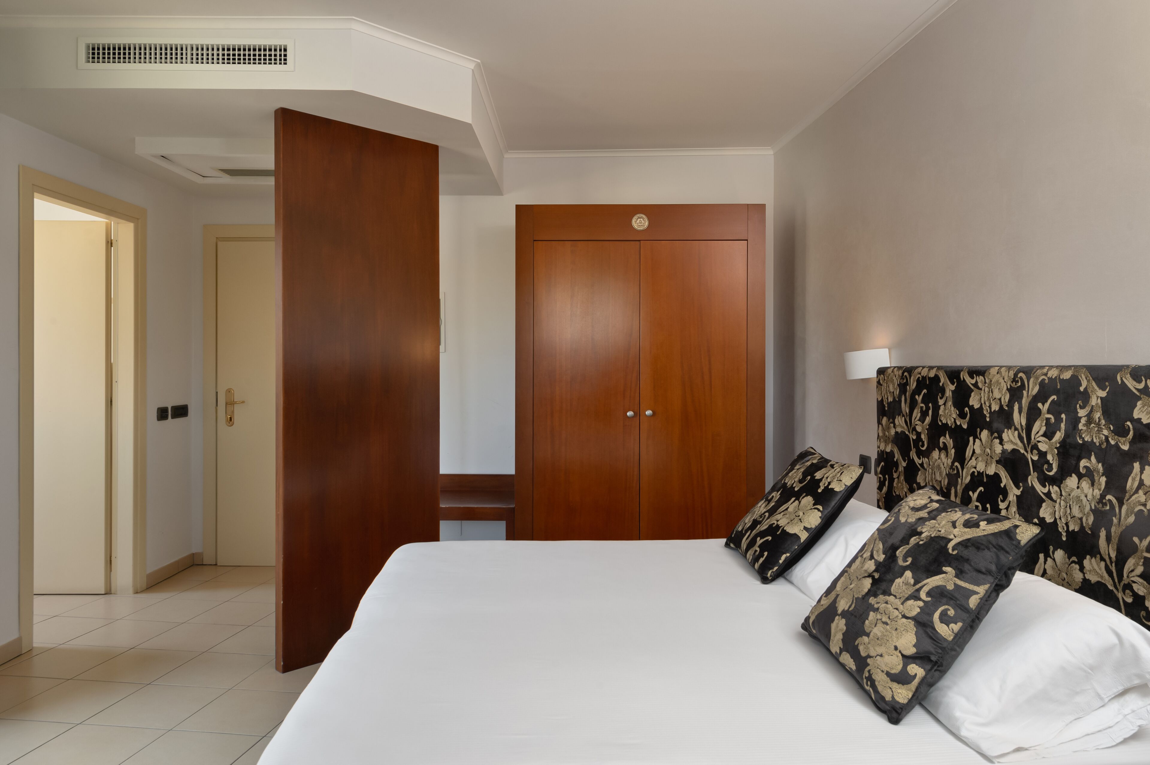 Quarto de hotel com cama, guarda-roupa e mesa de cabeceira.