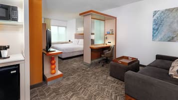 Quarto de hotel com cama, escrivaninha, sofá, televisão, micro-ondas e cafeteira.